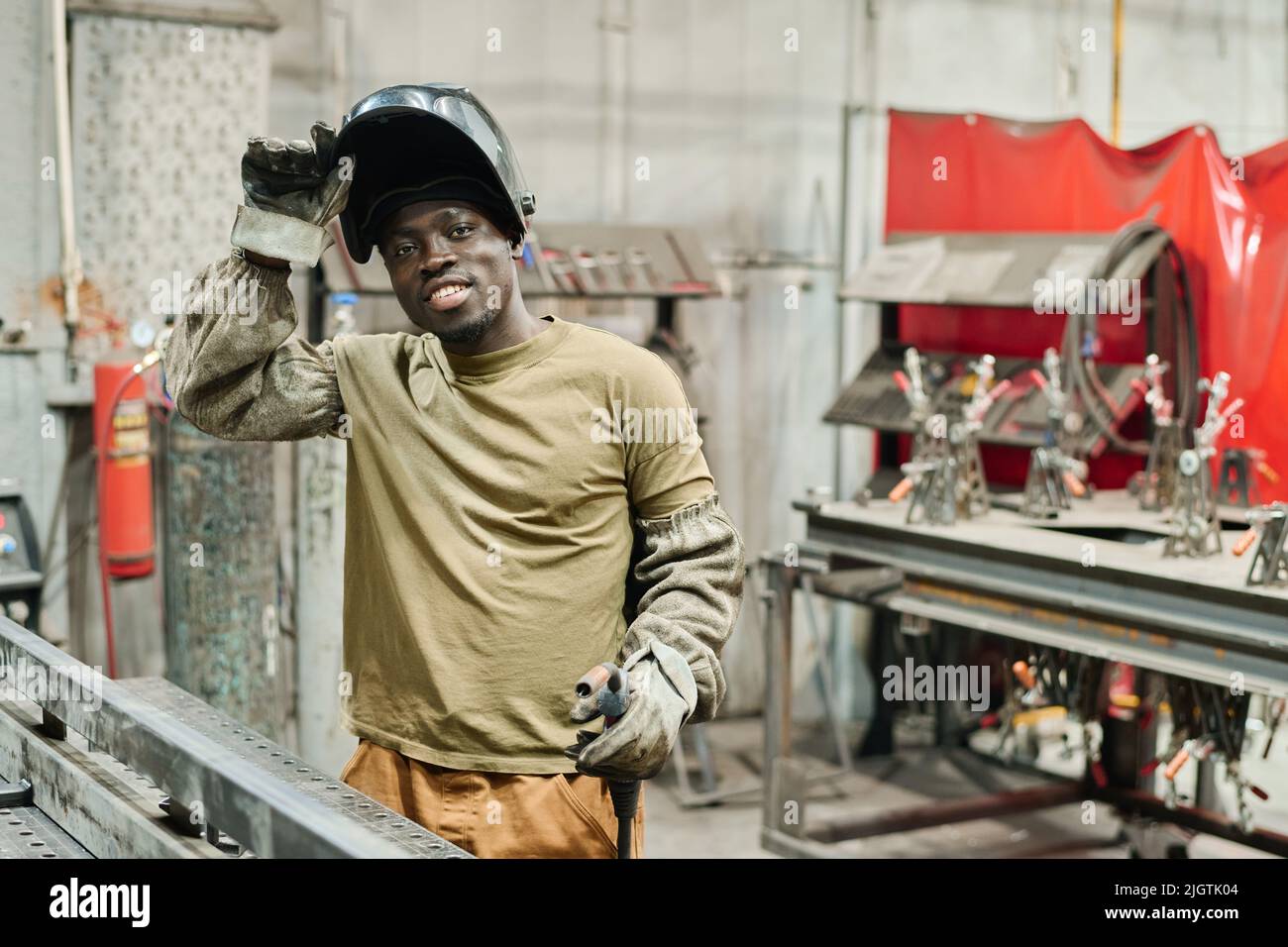 Portrait of African young welder in mask smiling at camera while ...