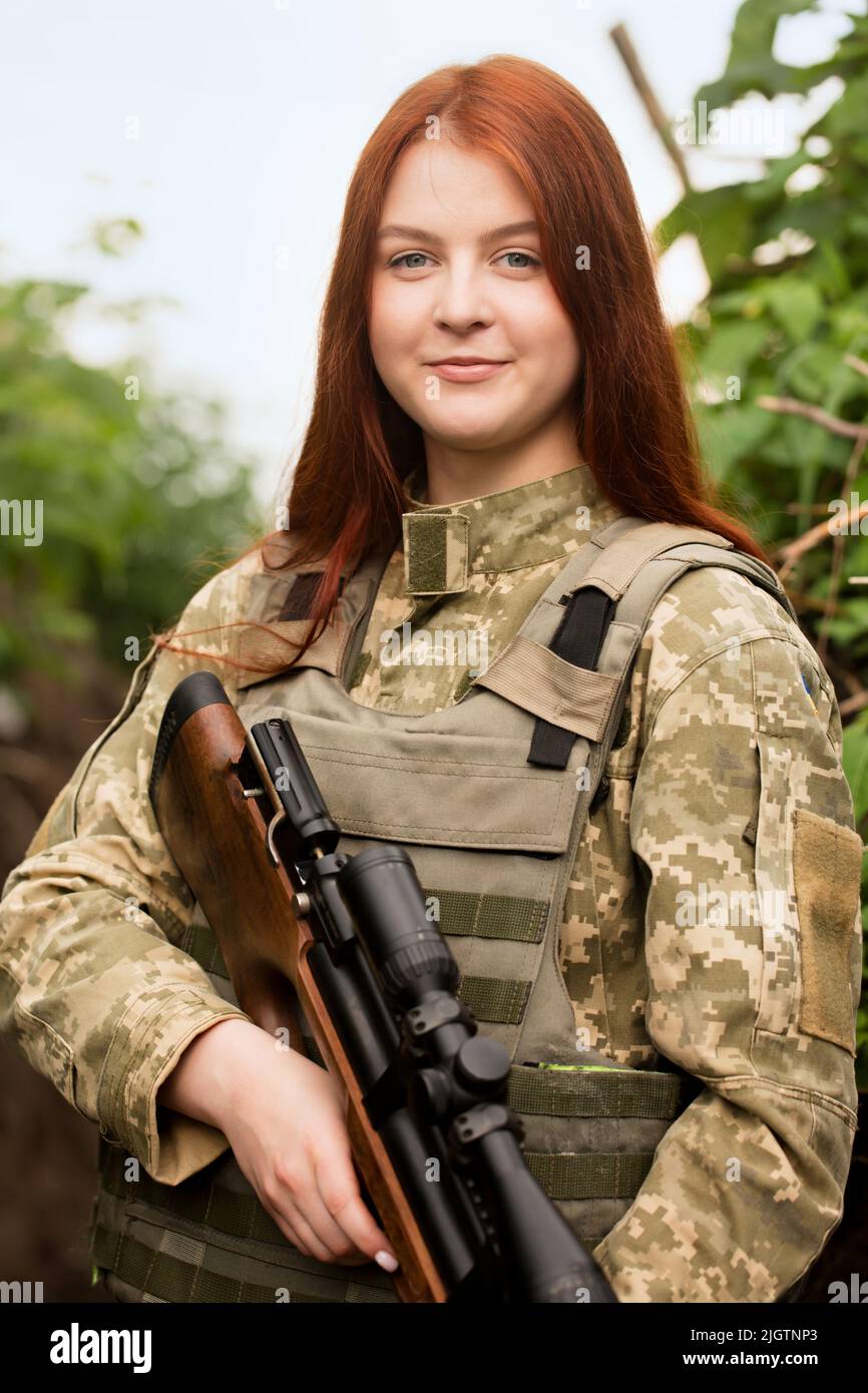 A beautiful red-haired girl in a bulletproof vest with a weapon in her ...