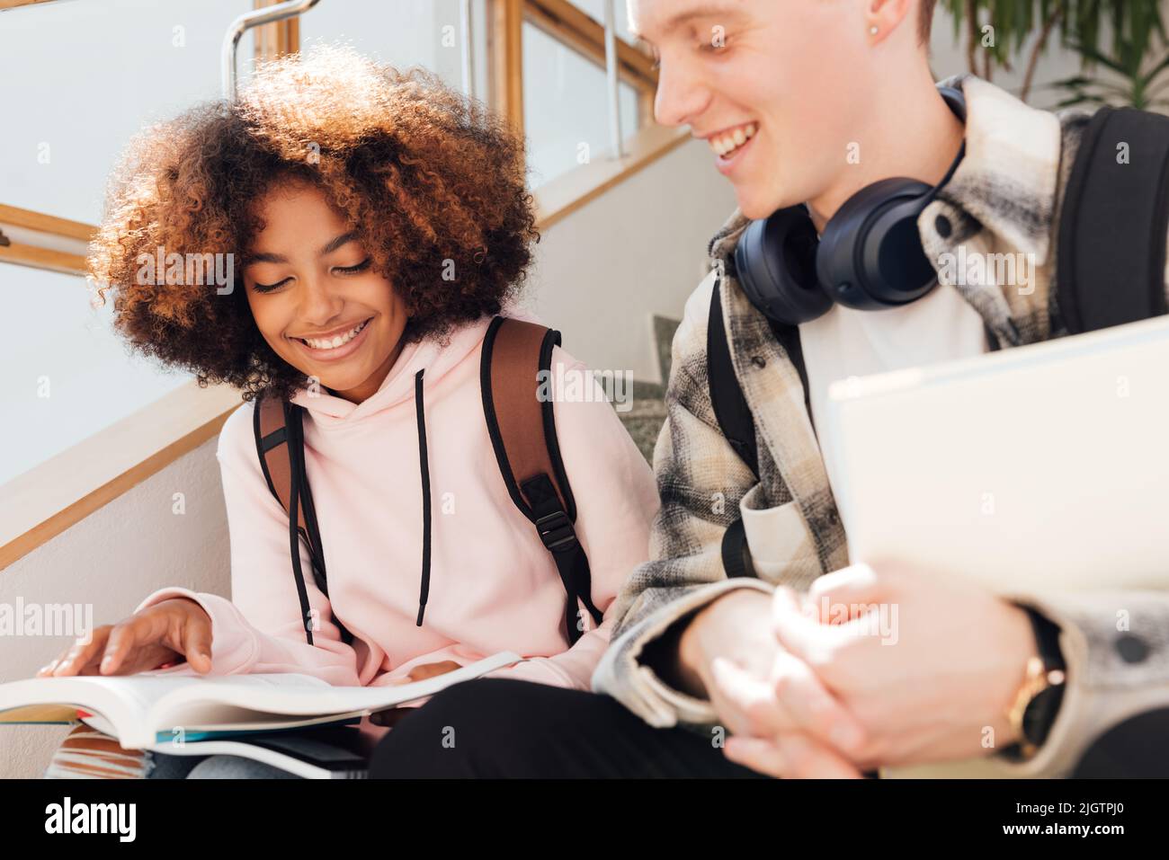 Two classmates are sitting on a stairs and reading. Boy and girl in ...