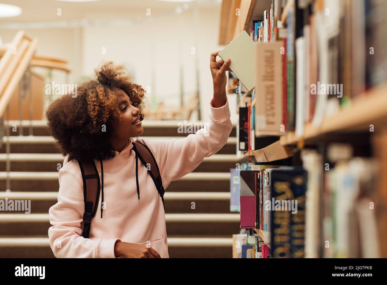 Girl taking a book from bookshelf in library Stock Photo - Alamy