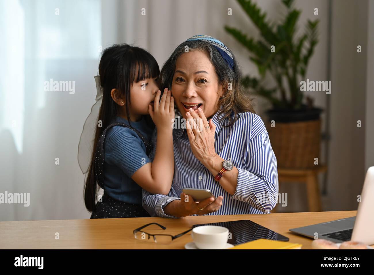 Cute little child whispering in ear, telling secret to grandmother ...