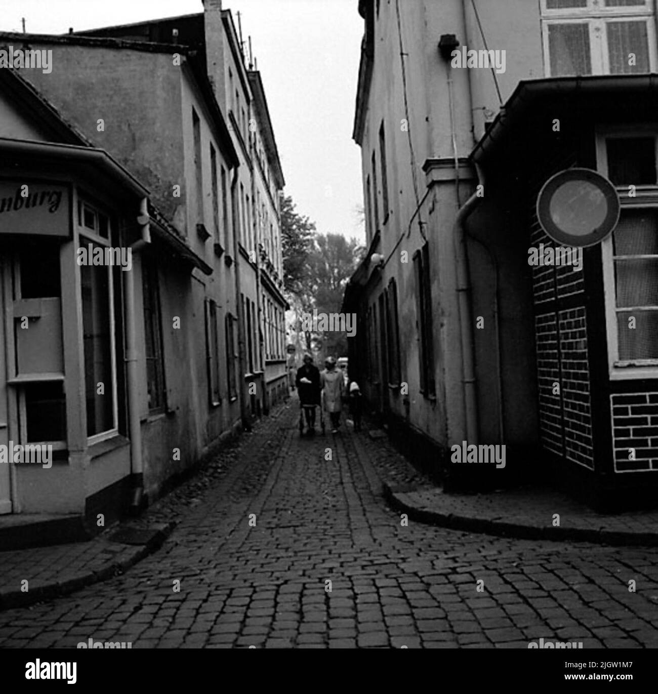 Two women and one child come walking on a paved street between ...