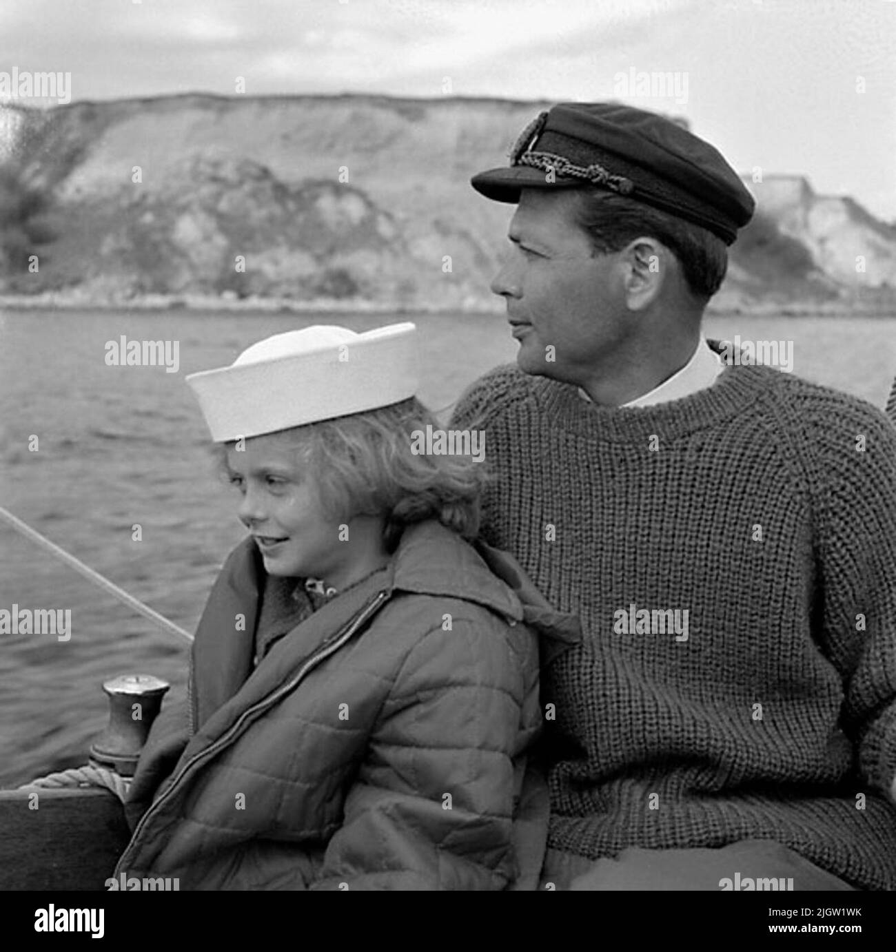 There is a man and a girl in the cockpit on a sailboat. The man holds ...