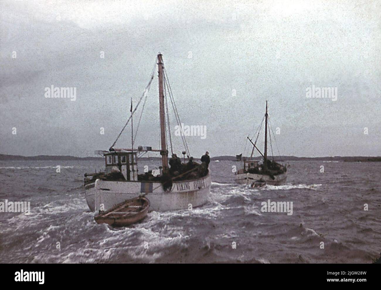 Two fishing boats out on the sea, they both pull a little dinghy behind ...