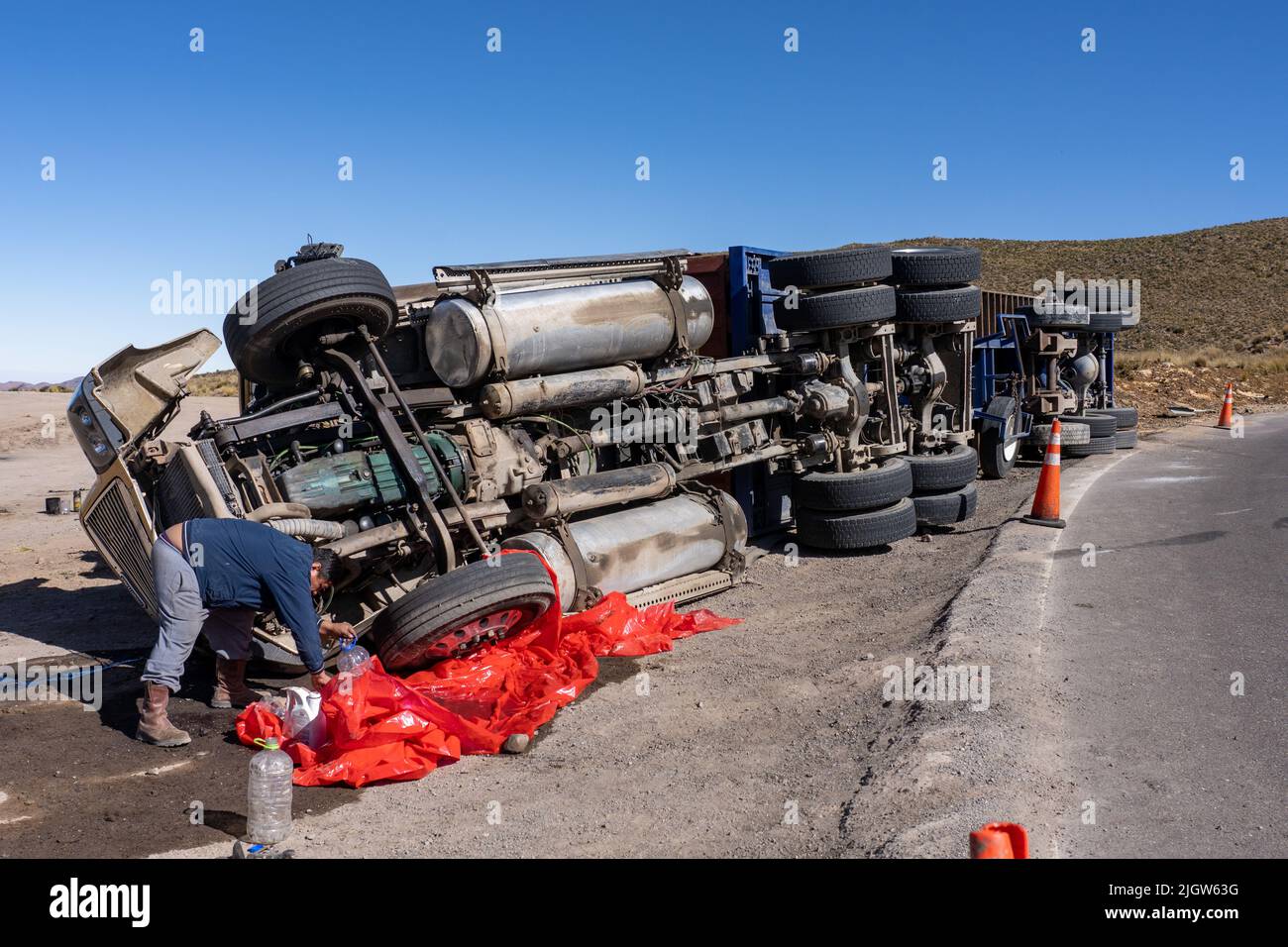 The driver of a crashed semi truck cleans up spilled diesel fuel ...