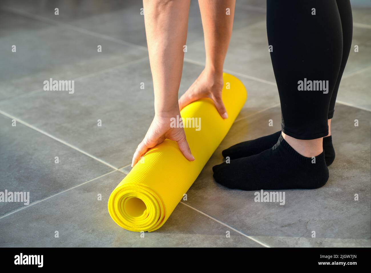 Girl is preparing to unwrap yellow roll of sports mat for yoga. Hands ...