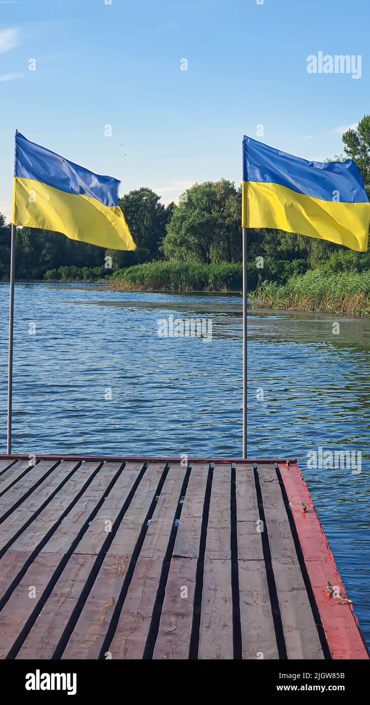 Ukrainian flags flutter on the pier of the river. Summer sunny day ...