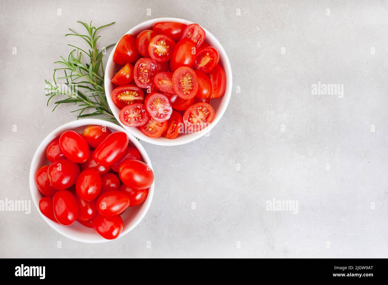 Bowls of small cut and uncut Rosa tomatoes on mottled grey with copy ...