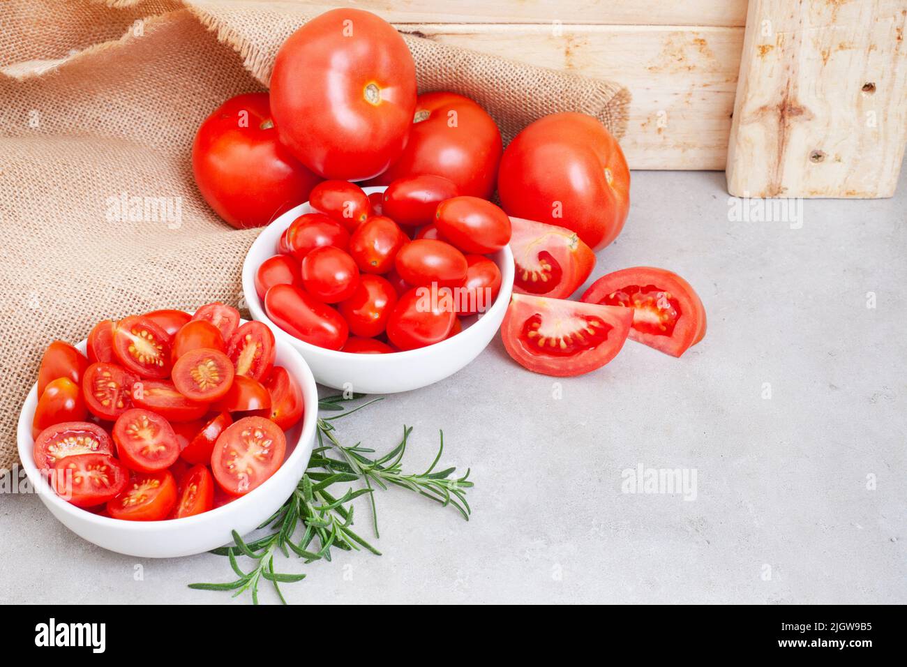 Bowls of small cut and uncut Rosa tomatoes on mottled grey with copy ...