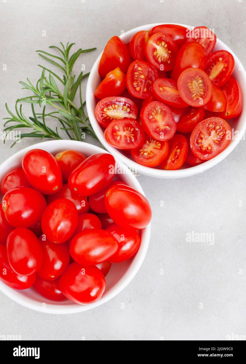 Bowls of small cut and uncut Rosa tomatoes on mottled grey with copy ...