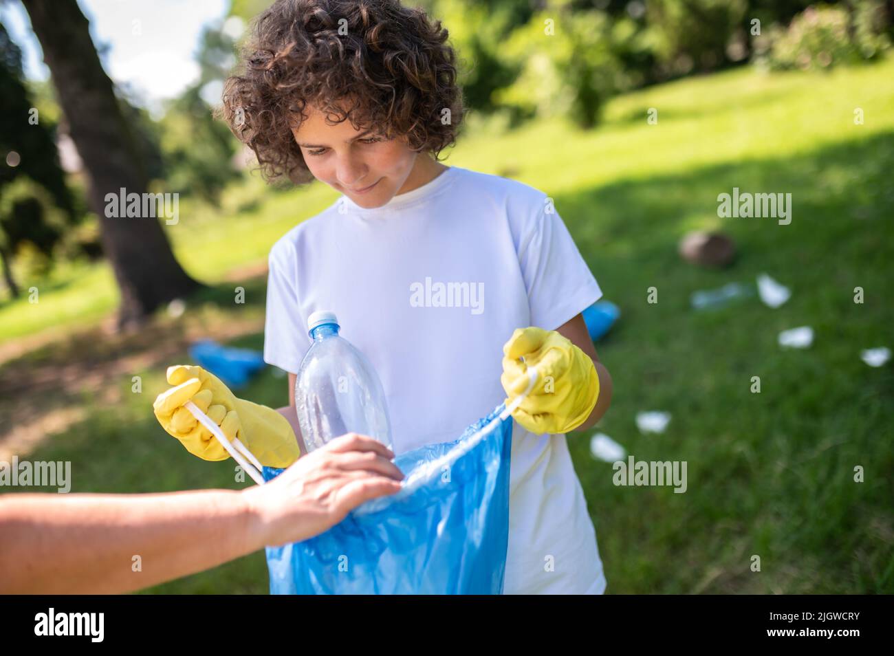 Someone helping a curly-haired teen to gather garbage Stock Photo - Alamy