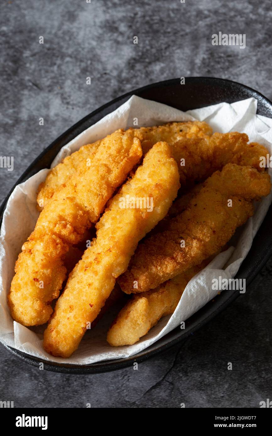 Breaded chicken fillet strips on a paper towel in a black bowl. On a ...