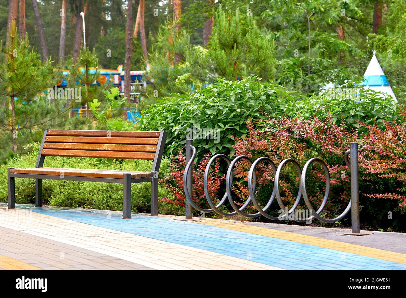 Wooden bench and bike rack in a green city park with rides and trees ...