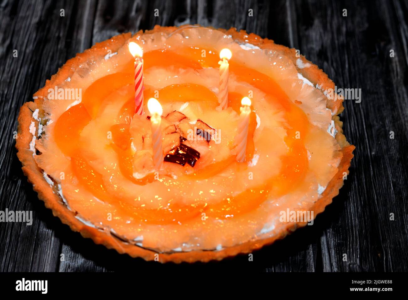 A fruit tart cake with birthday candles with fresh pieces of apple ...