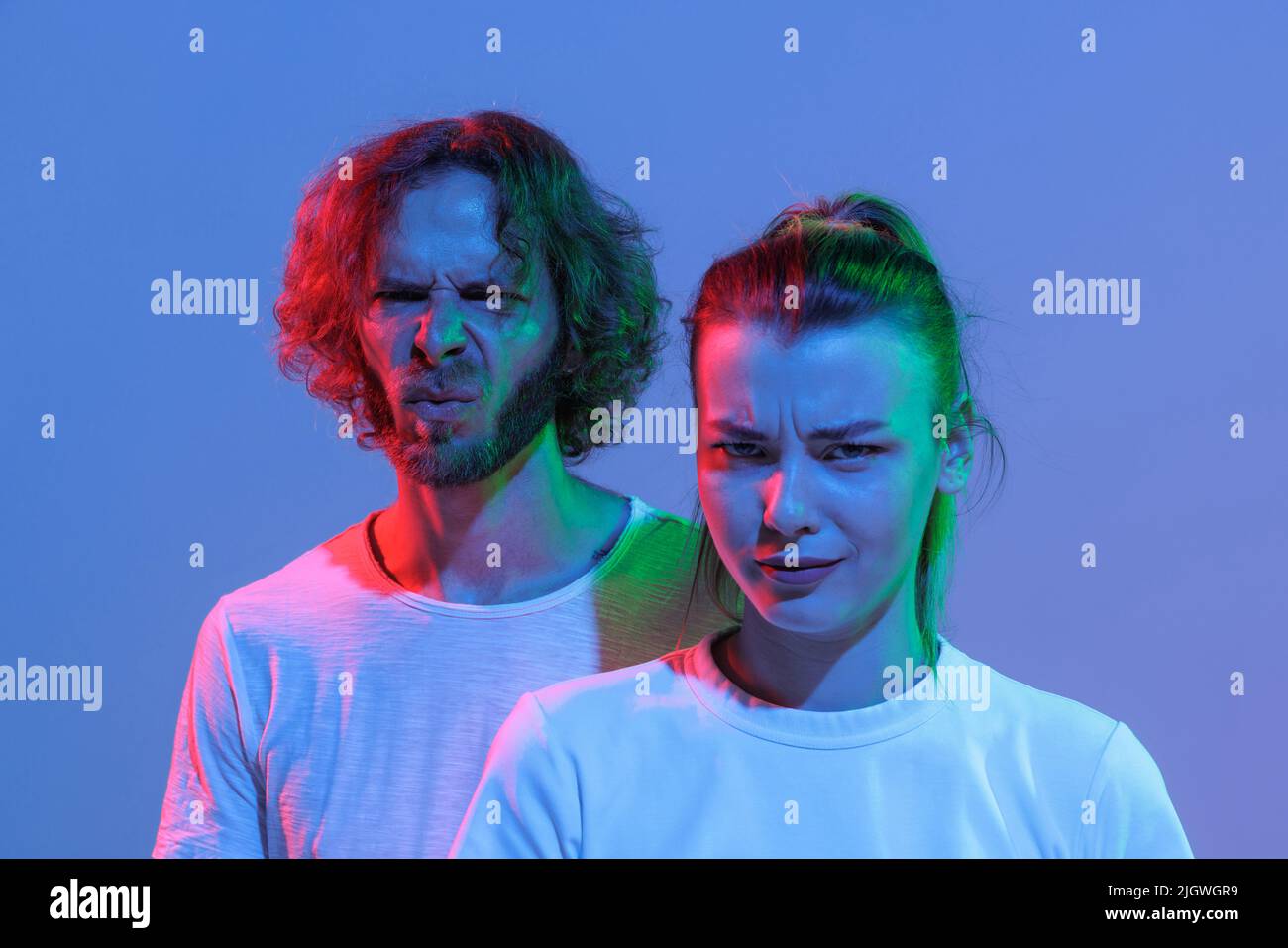 Portrait of young man and woman posing isolated over blue background in ...