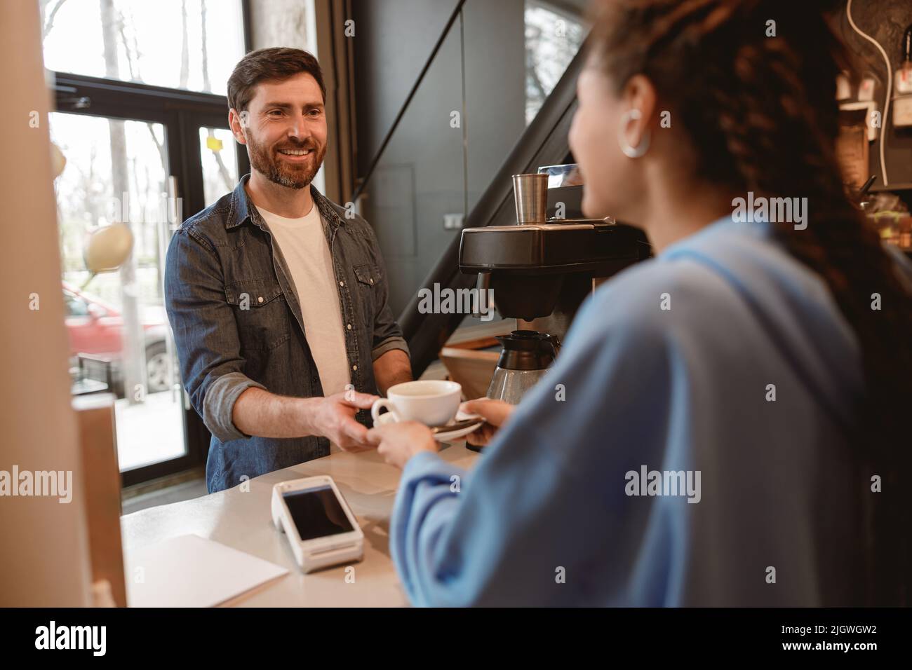 Female barista serving coffee at bar and giving cup to male customer ...