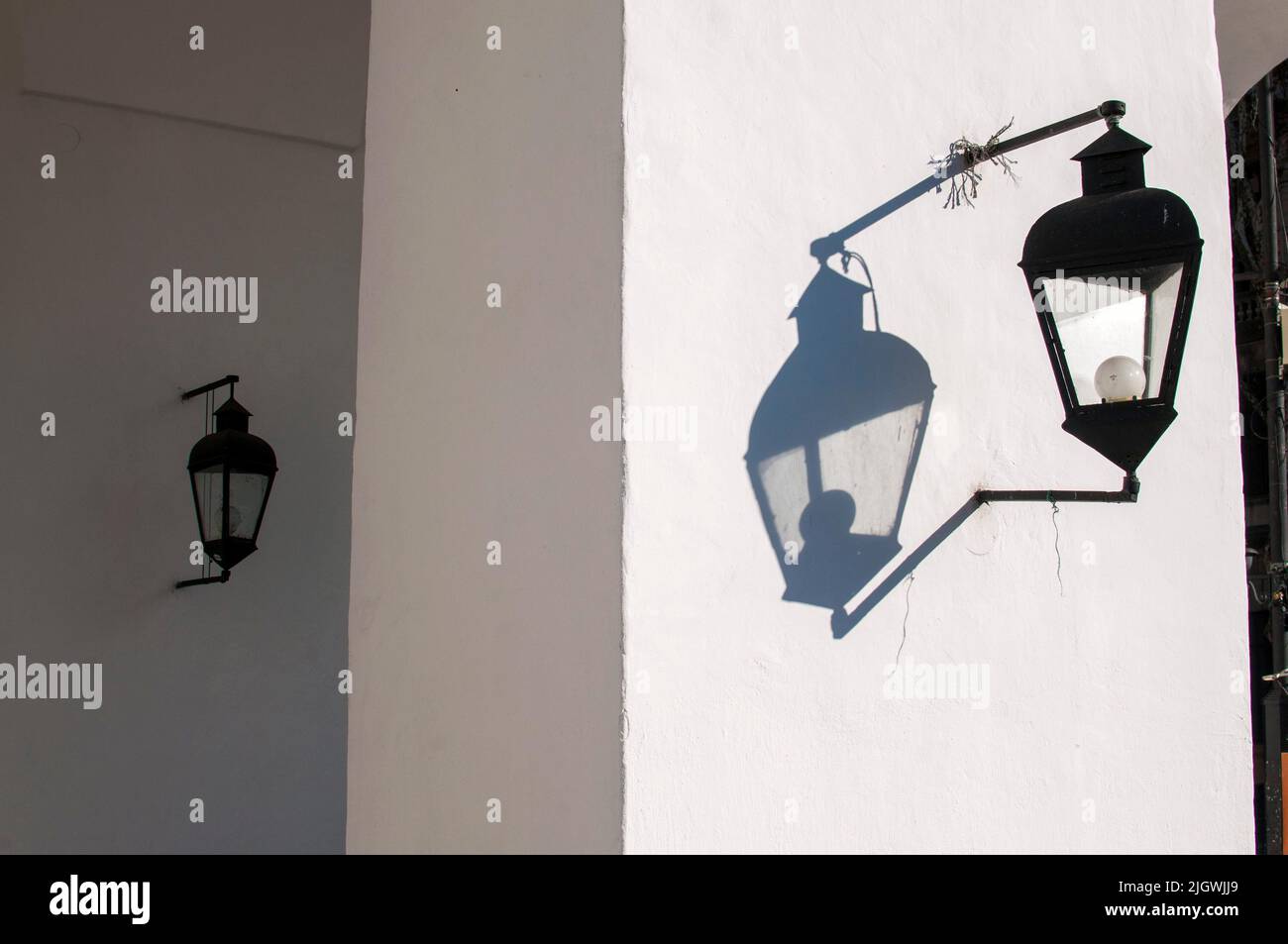 A closeup of a lamppost hanging on a white building with its shadow on ...