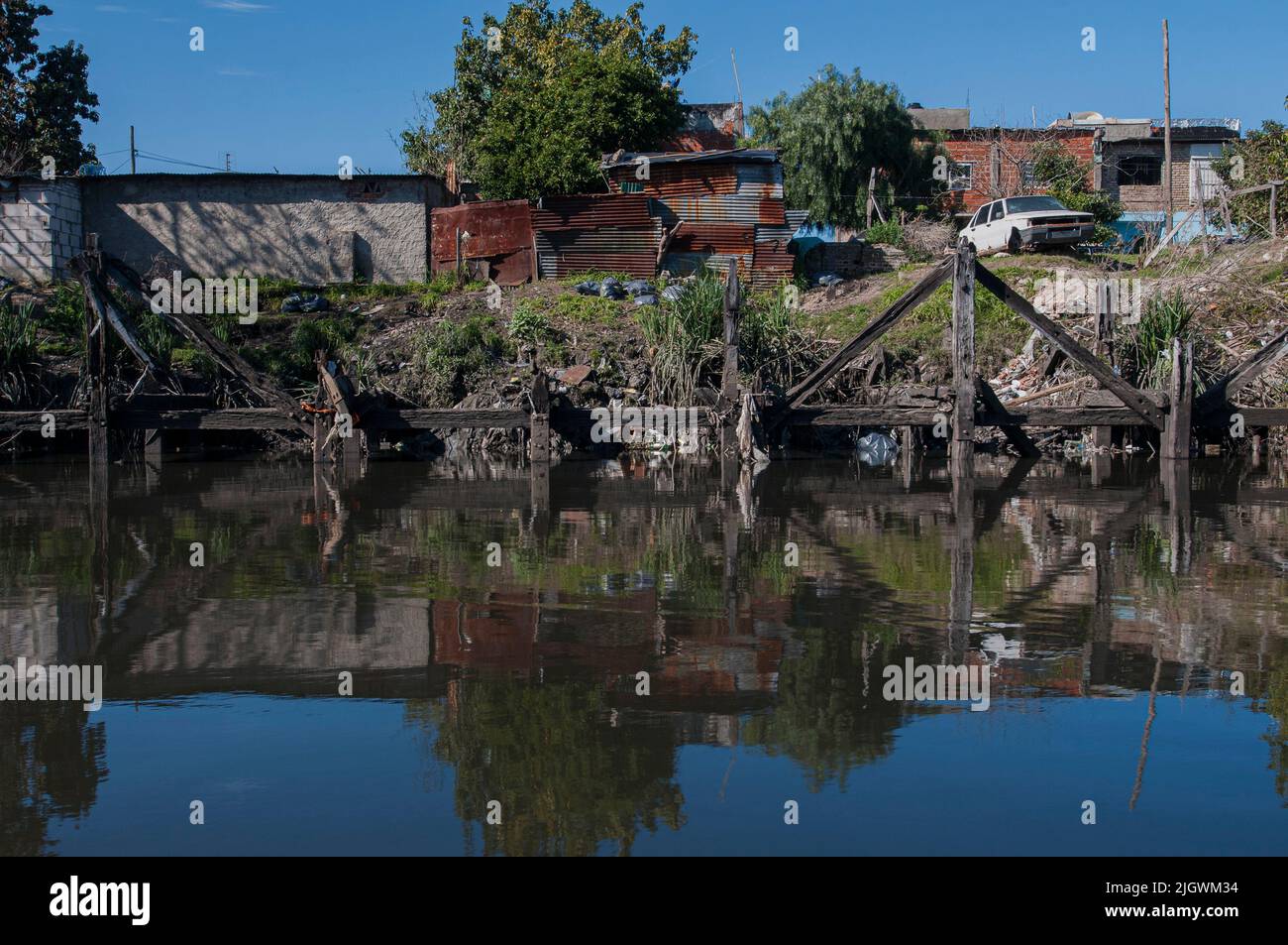 A slum and green trees reflecting in the Riachuelo river in Argentina ...