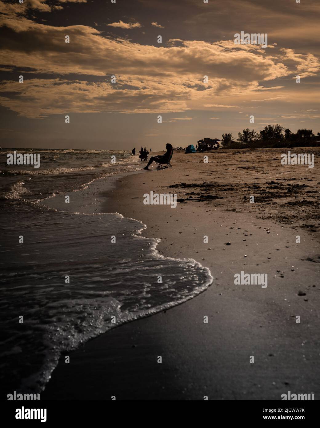 A vertical shot of people against sea waves washing a sandy beach Stock ...