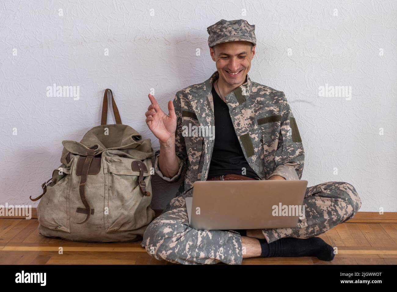 Happy army soldier having video call over laptop and waving to someone ...