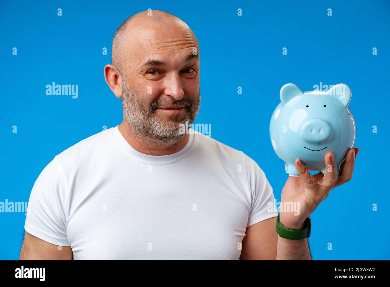Middle-aged man holding piggy bank against blue background Stock Photo ...