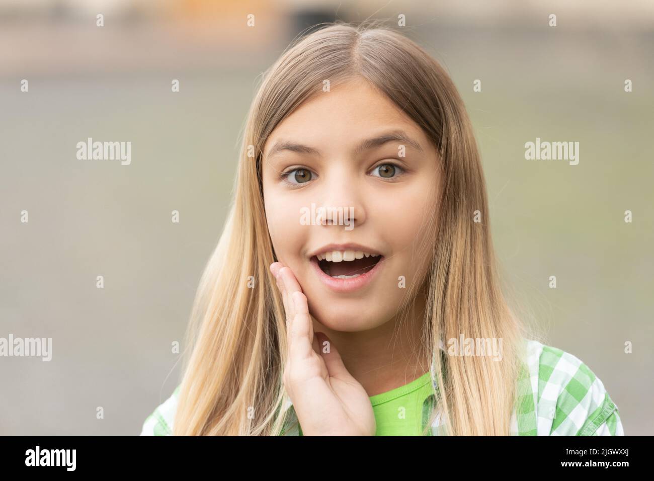 Portrait of tween girl with surprised face holding hand on cheek blurry ...