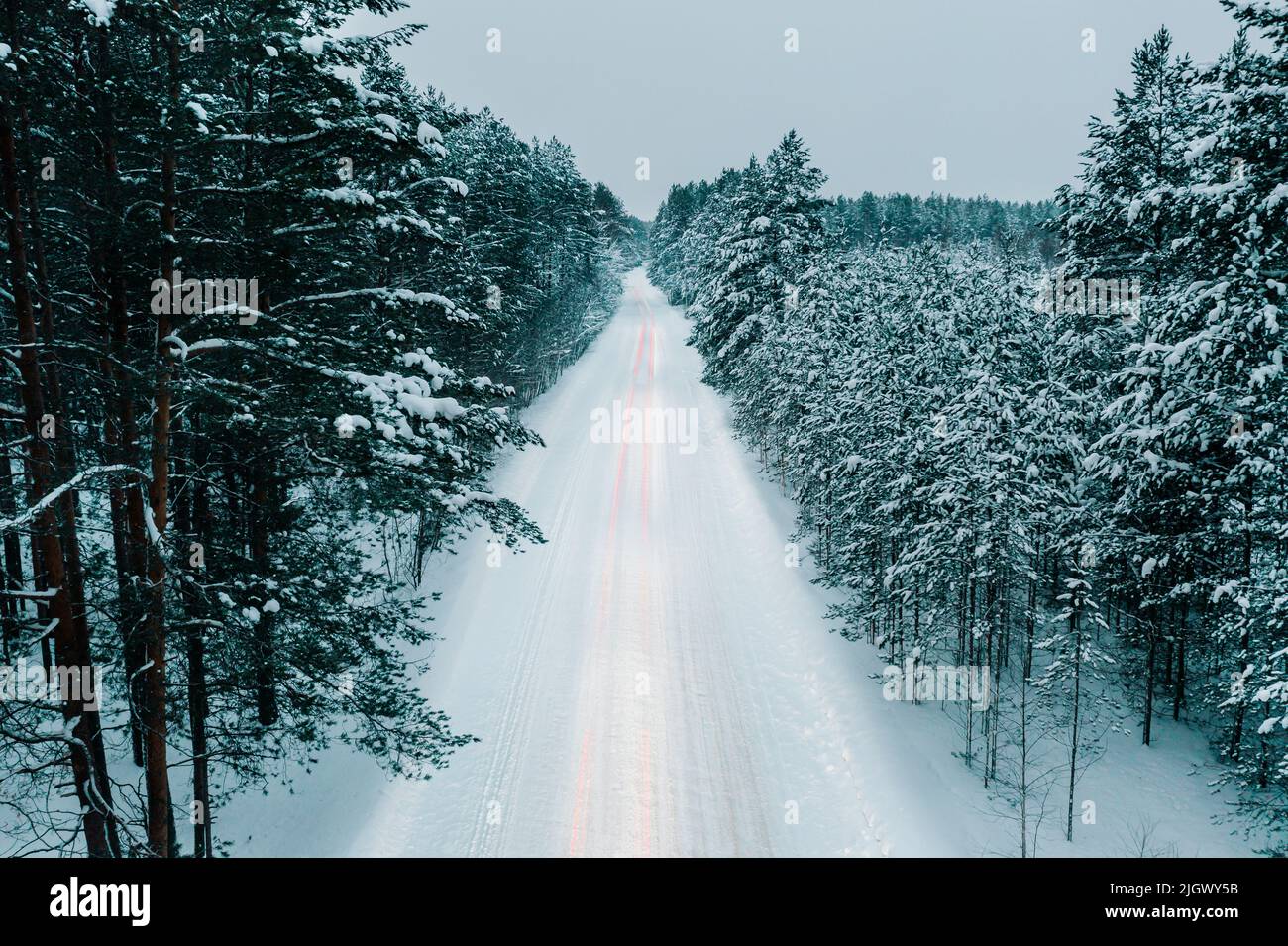 Aerial drone view of snowy winter road in forest with light lines from ...