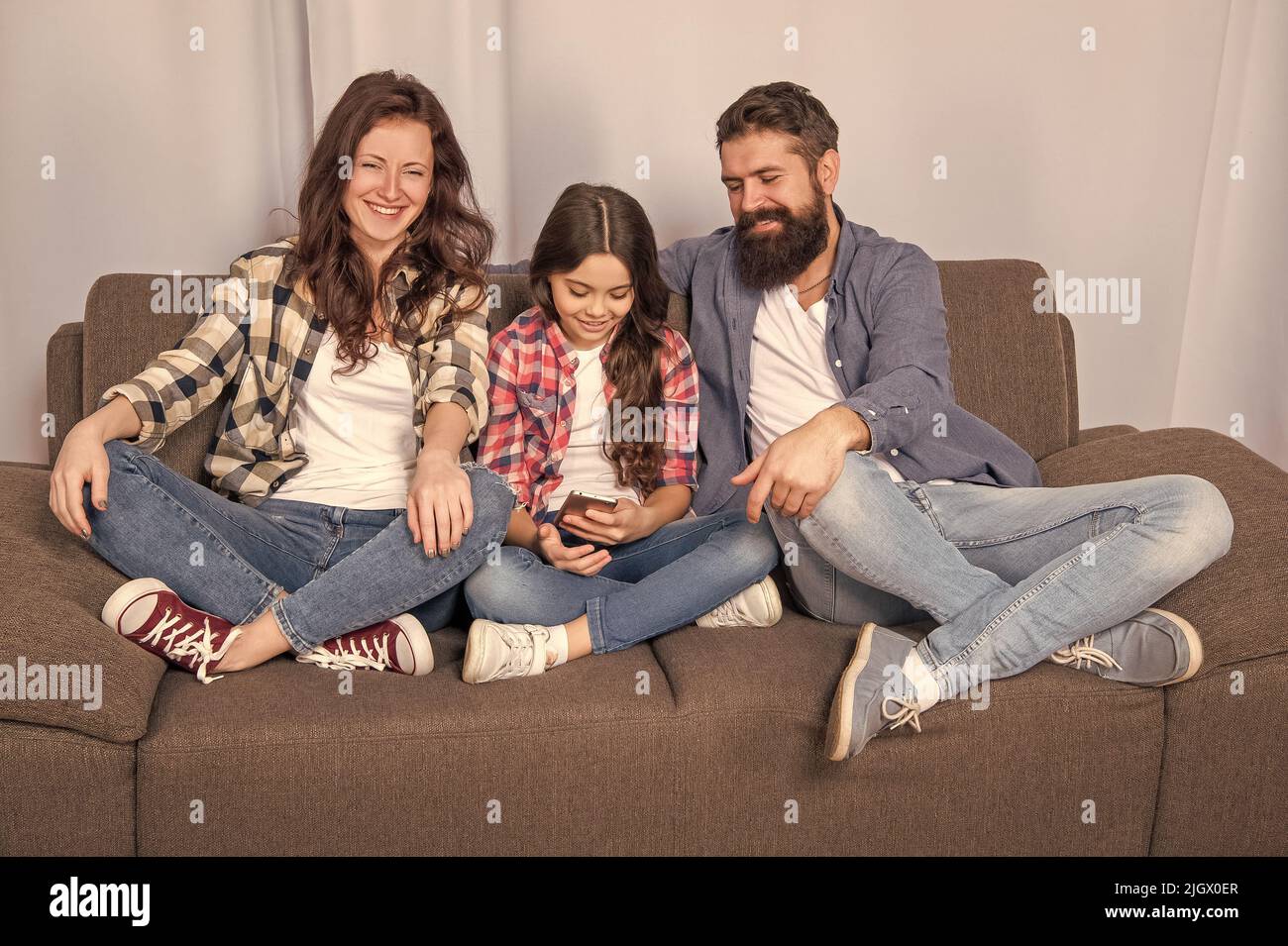 Smartphone obsessed kid. Child use mobile phone sitting next to parents ...