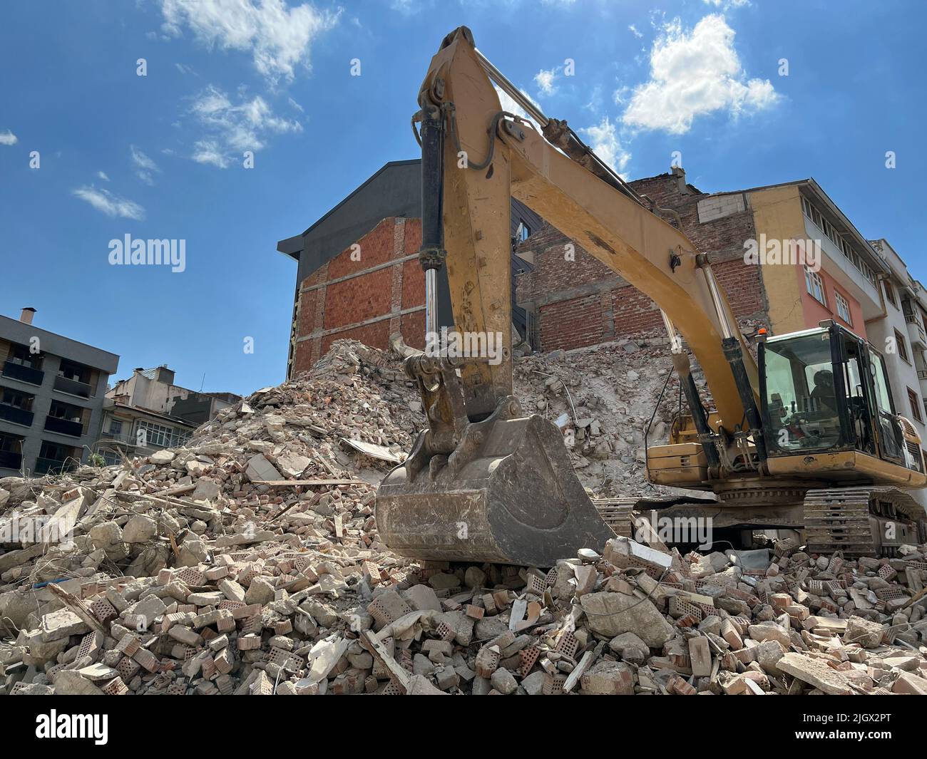 Hydraulic Excavator is on the rubble of the building it demolished ...
