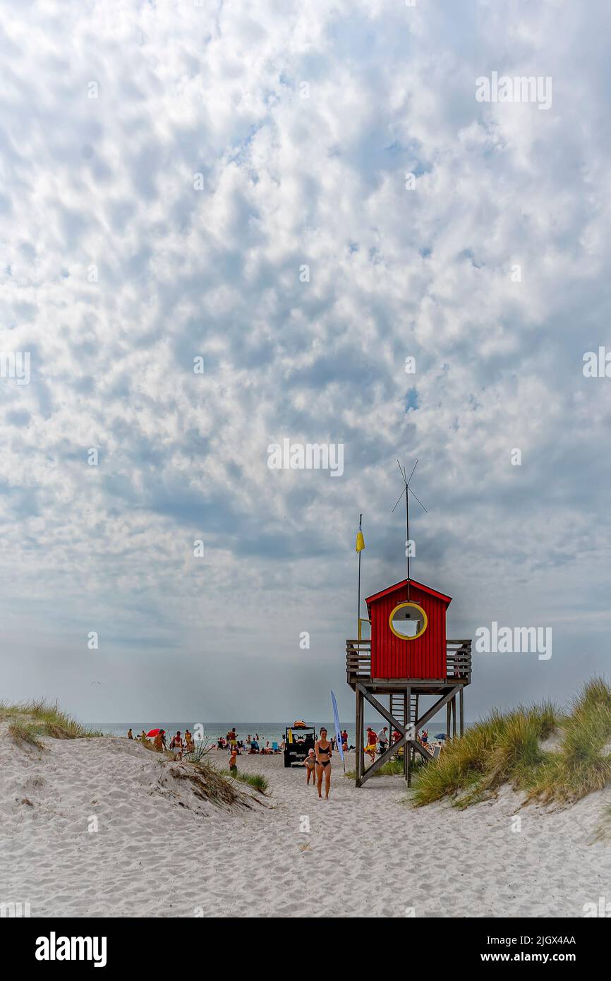 A vertical shot of a red lifeguard post and people enjoying the beach ...