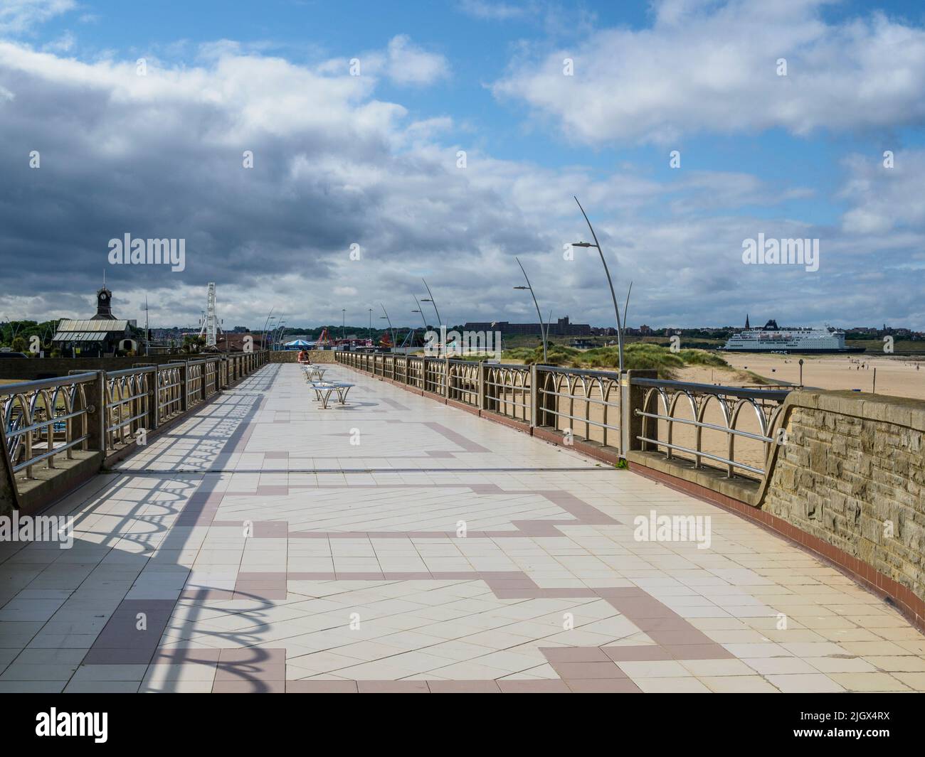 A walkway with metal seats and tiles on the beach in cloudy sky ...