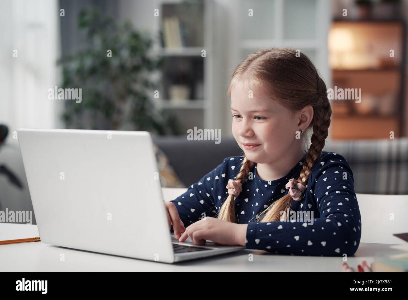 Cute little girl looking at monitor of laptop and typing at table ...