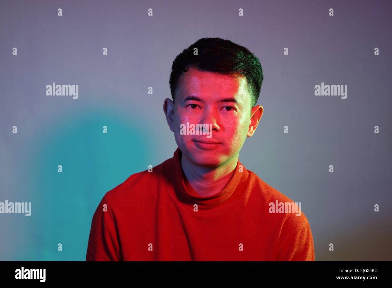 The cool adult Asian man on the blue background under the color gel ...