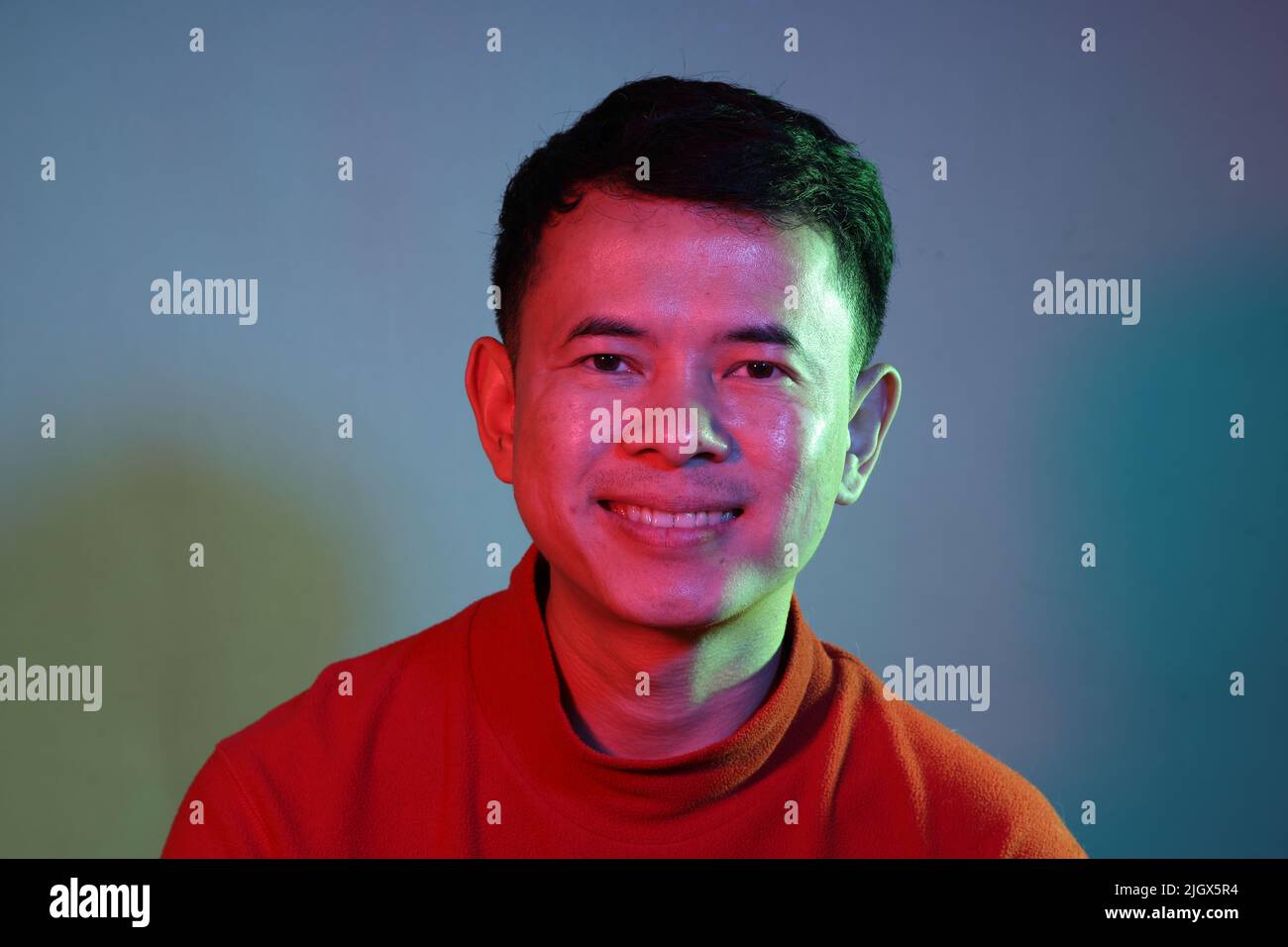 The cool adult Asian man on the blue background under the color gel ...