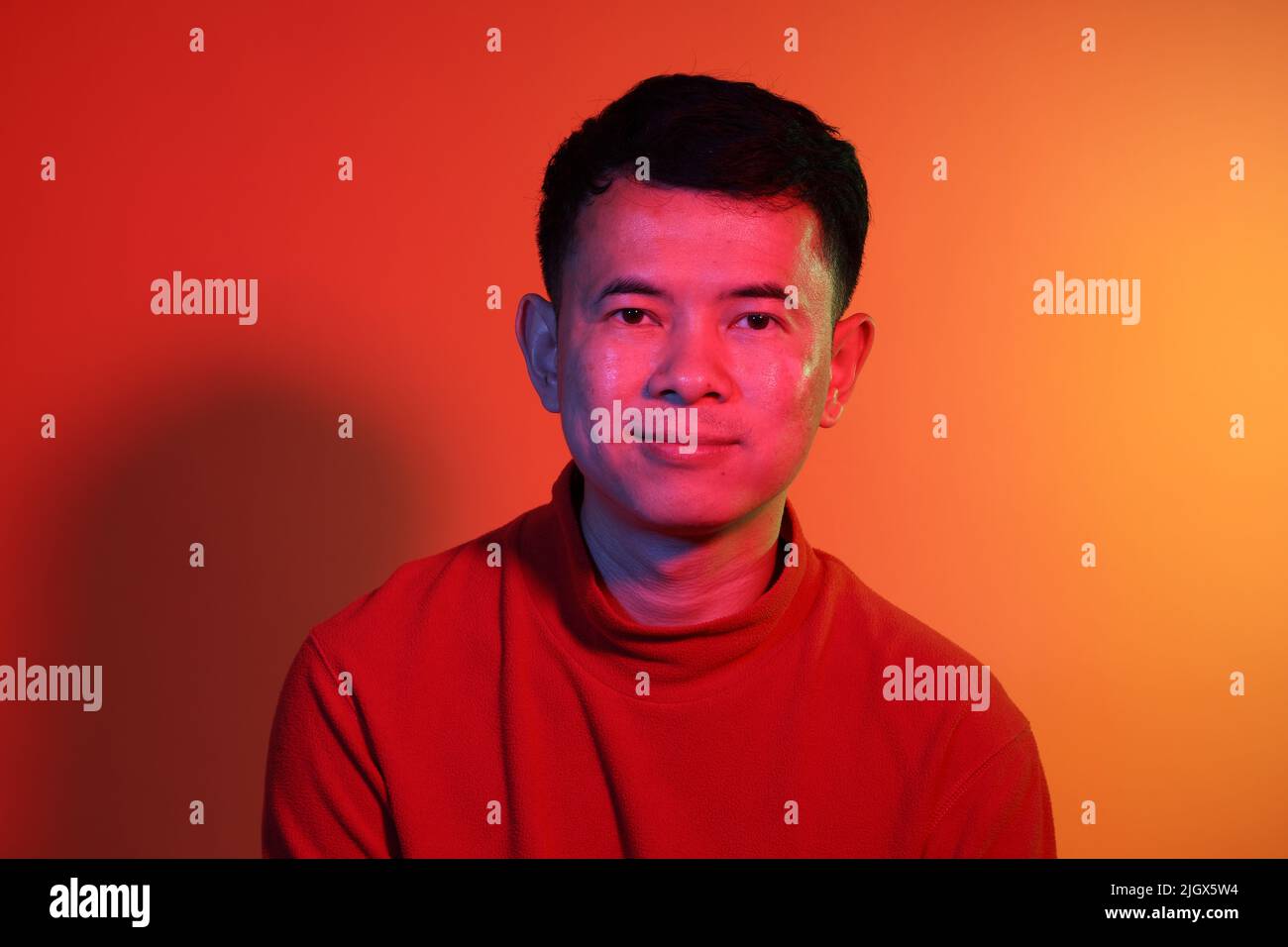The cool adult Asian man on the blue background under the color gel ...