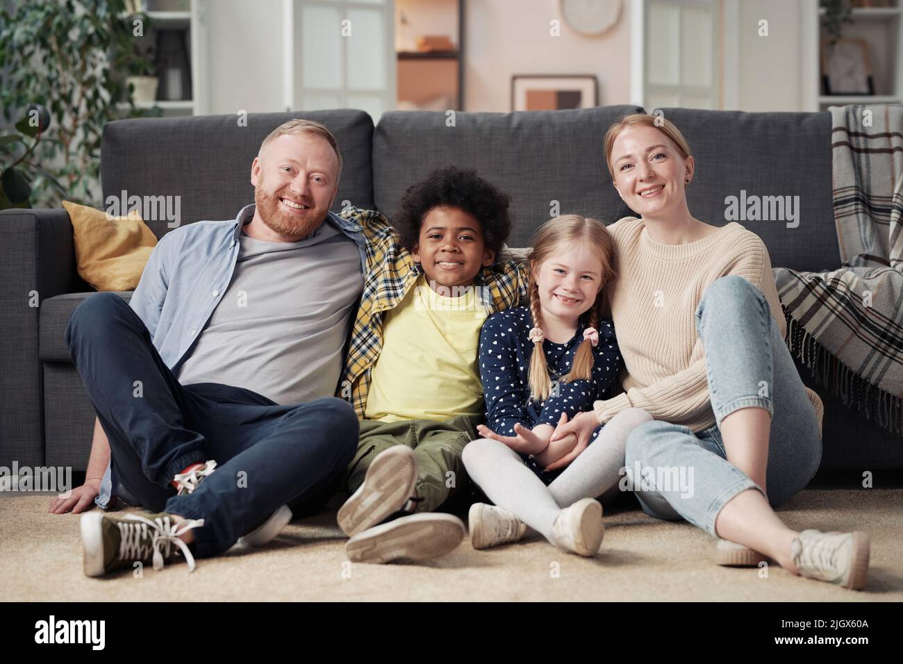 Portrait of happy foster parents sitting on floor with their adopted ...