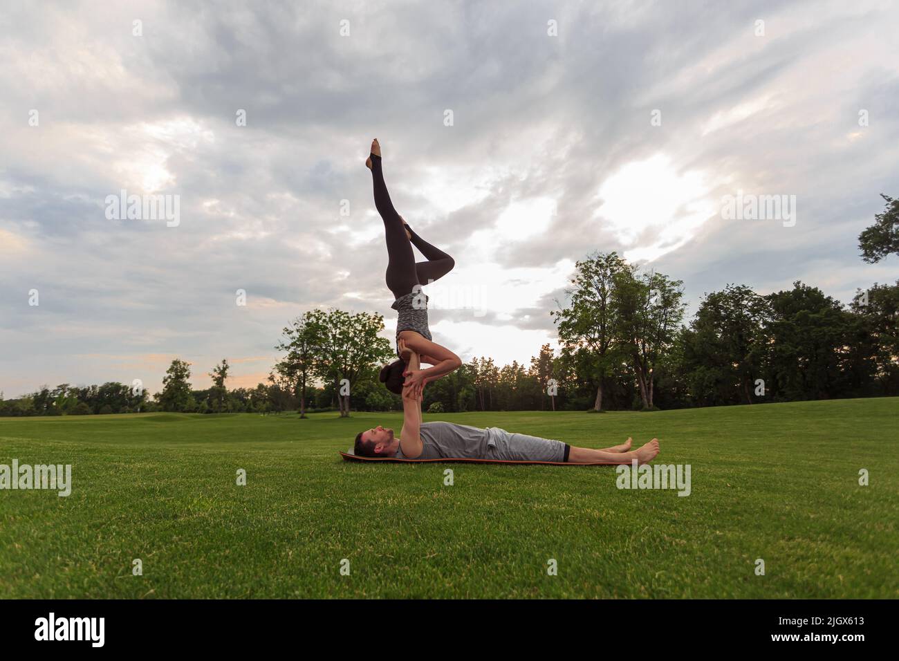Healthy man lying on grass and balancing woman. Couple doing acrobatic ...