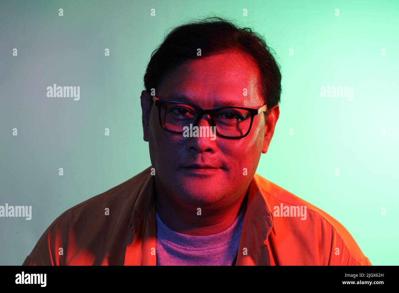 The cool adult Asian man on the blue background under the color gel ...