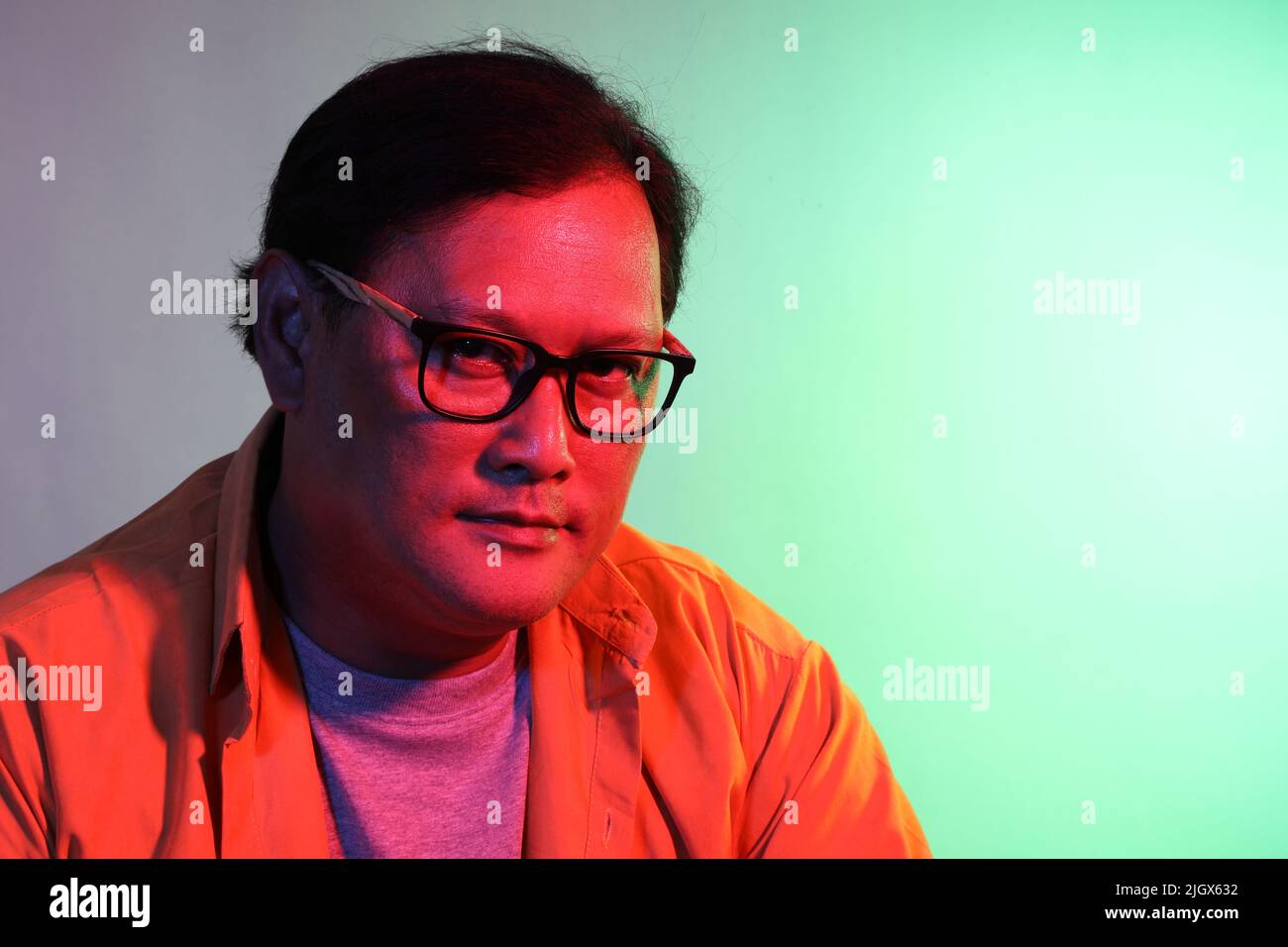 The cool adult Asian man on the blue background under the color gel ...