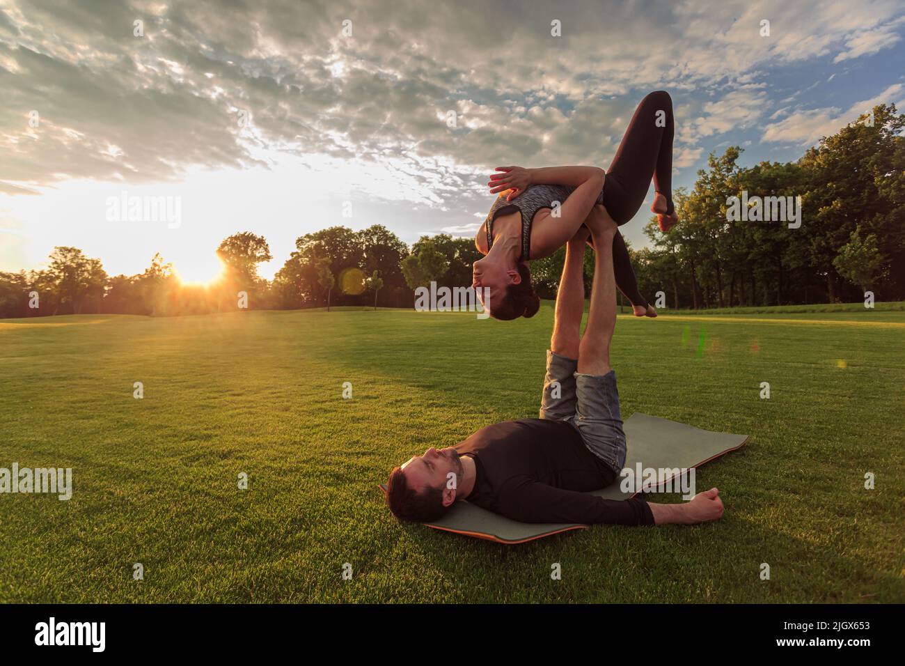 Man lying on grass and balancing woman in his feet. Young couple doing ...