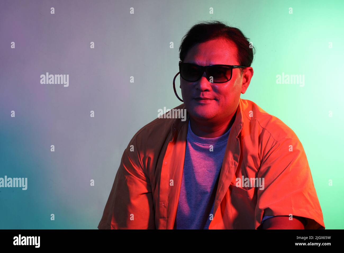 The cool adult Asian man on the blue background under the color gel ...