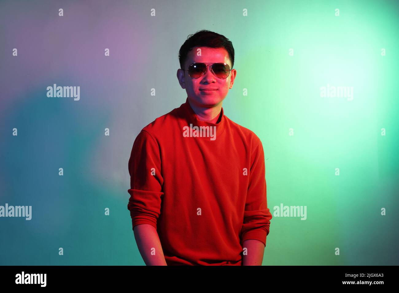 The cool adult Asian man on the blue background under the color gel ...