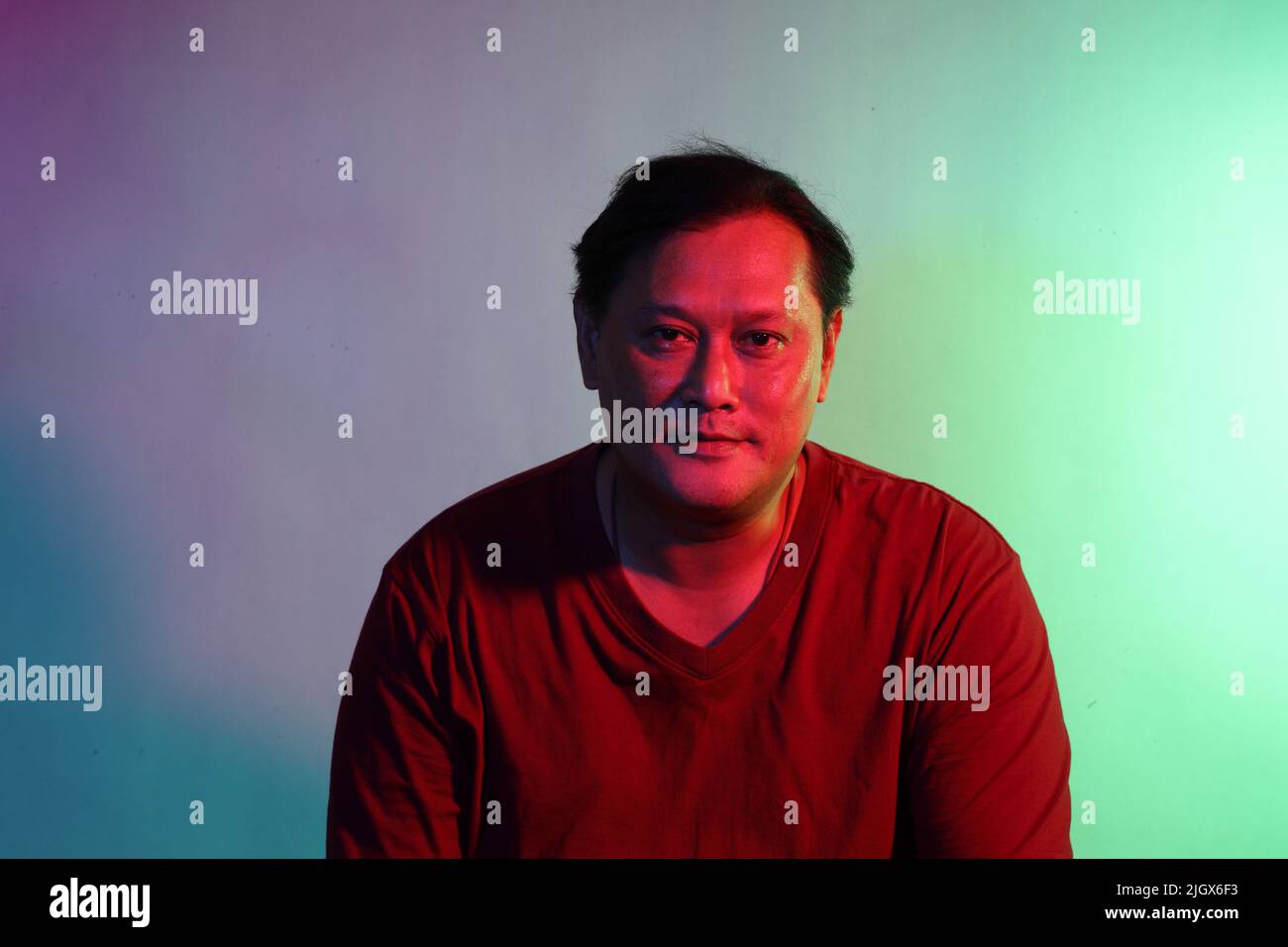 The cool adult Asian man on the blue background under the color gel ...