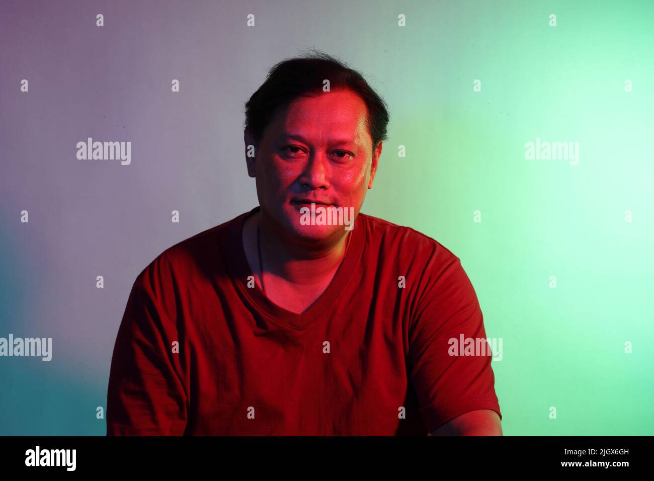 The cool adult Asian man on the blue background under the color gel ...