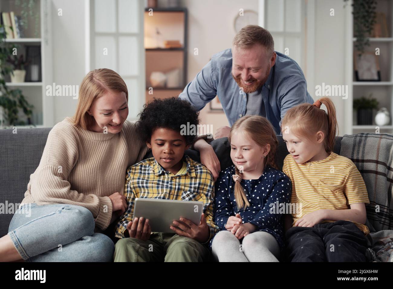 Happy parents spending time with their adopted children using digital ...