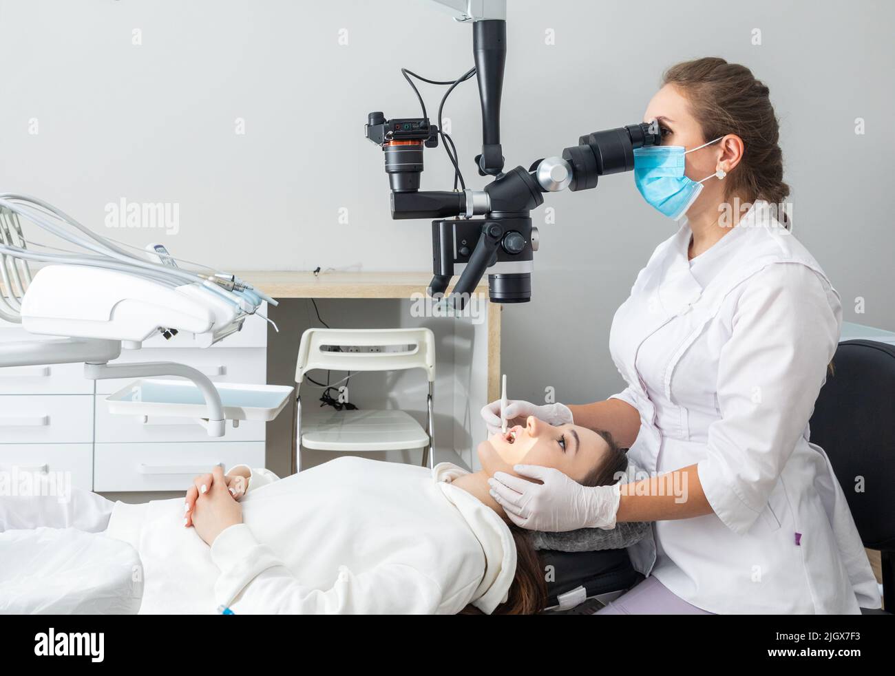 Female dentist using dental microscope treating patient teeth at dental clinic office. Medicine ...