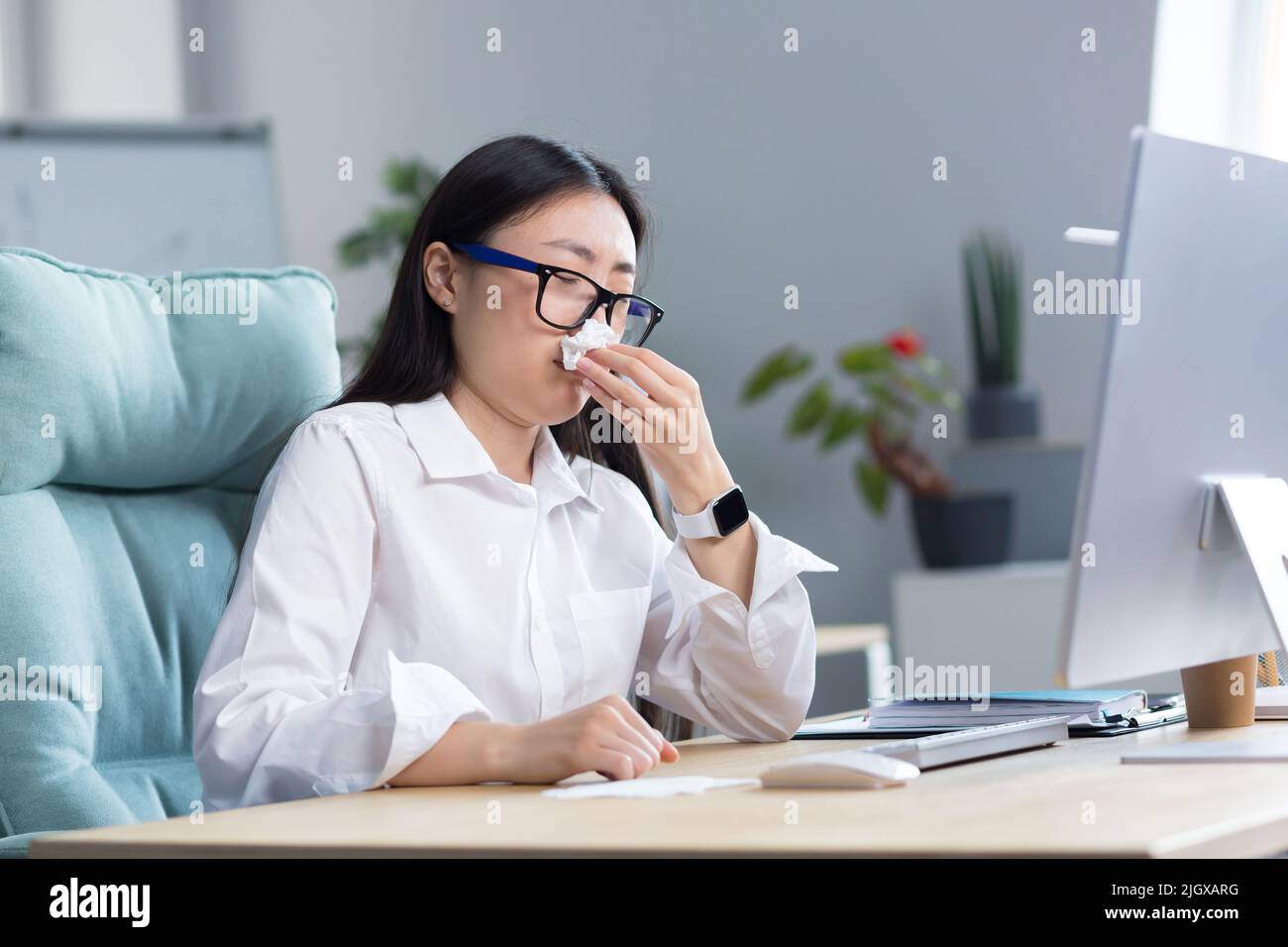 Feeling unwell at the workplace. A young beautiful Asian business woman ...