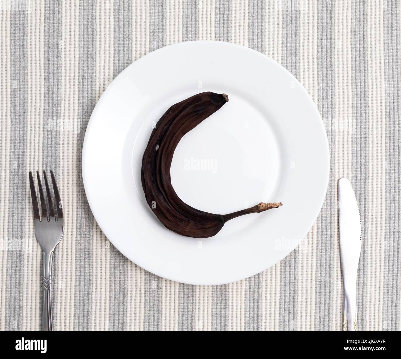 Black dried banana with mold on white plate with fork and knife. Hungry ...