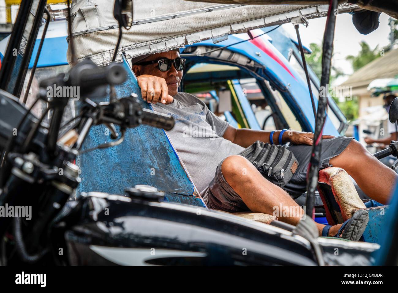A motorcycle "trike" (tricycle) driver takes a break while waiting for ...