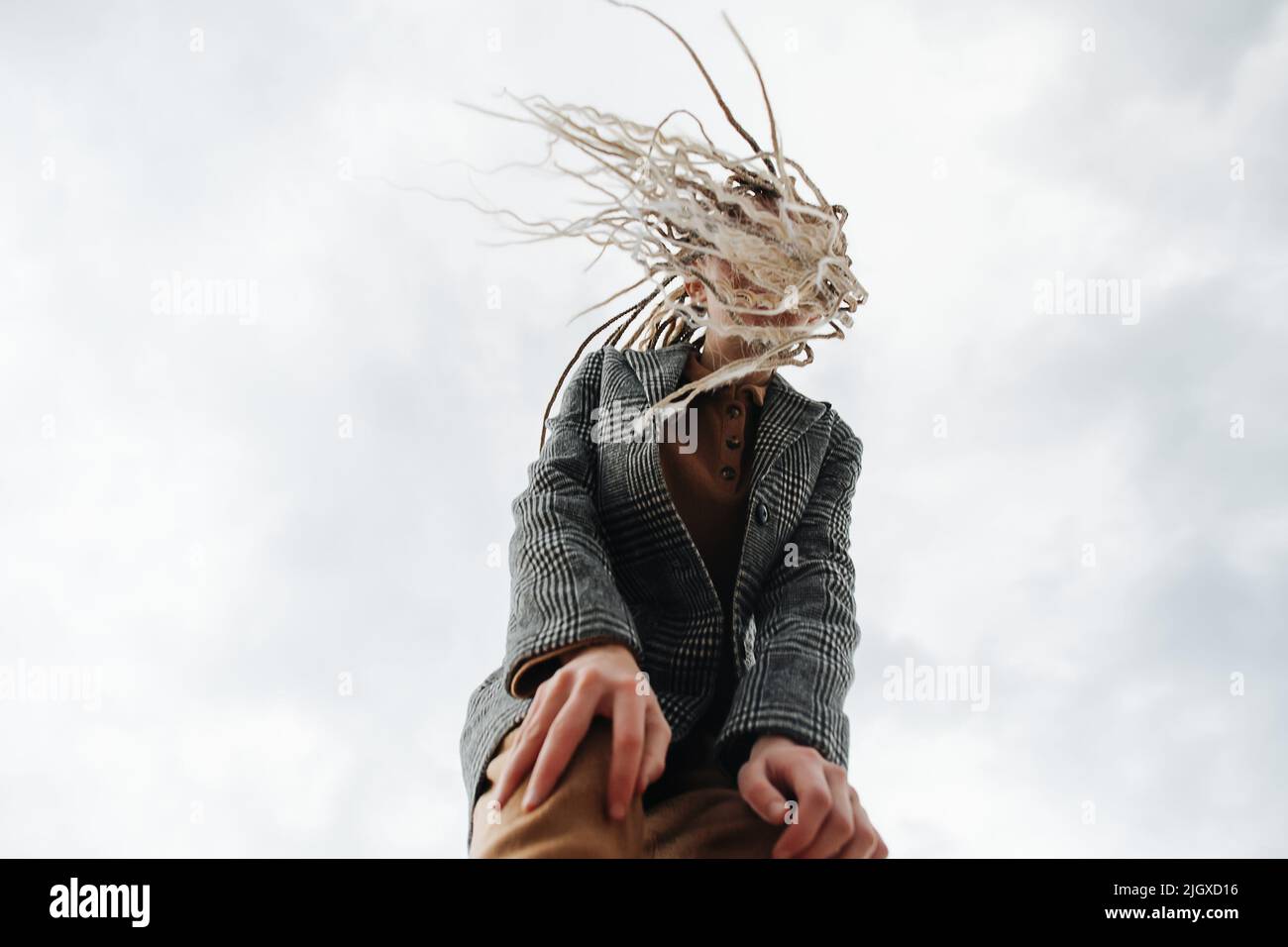 Upward image of a teenage girl shaking her dreads, against a grey sky ...